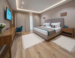 Quarto de hotel moderno com uma cama grande, escrivaninha, cadeira e televisão fixada na parede.