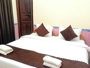 Cama bem arrumada com roupa de cama branca e marrom, cabeceira marrom e uma porta à esquerda.