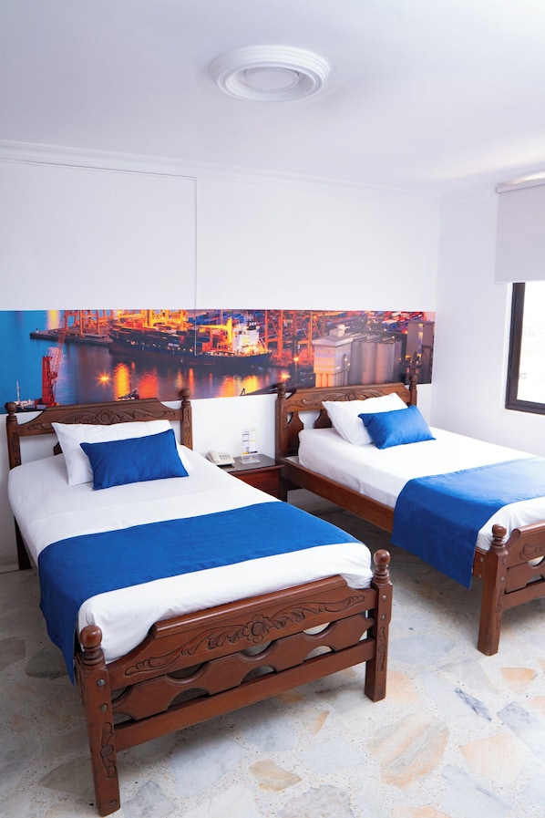 Duas camas de madeira com roupa de cama azul e branca, uma mesa de cabeceira com um telefone e um grande quadro com vista para a cidade.