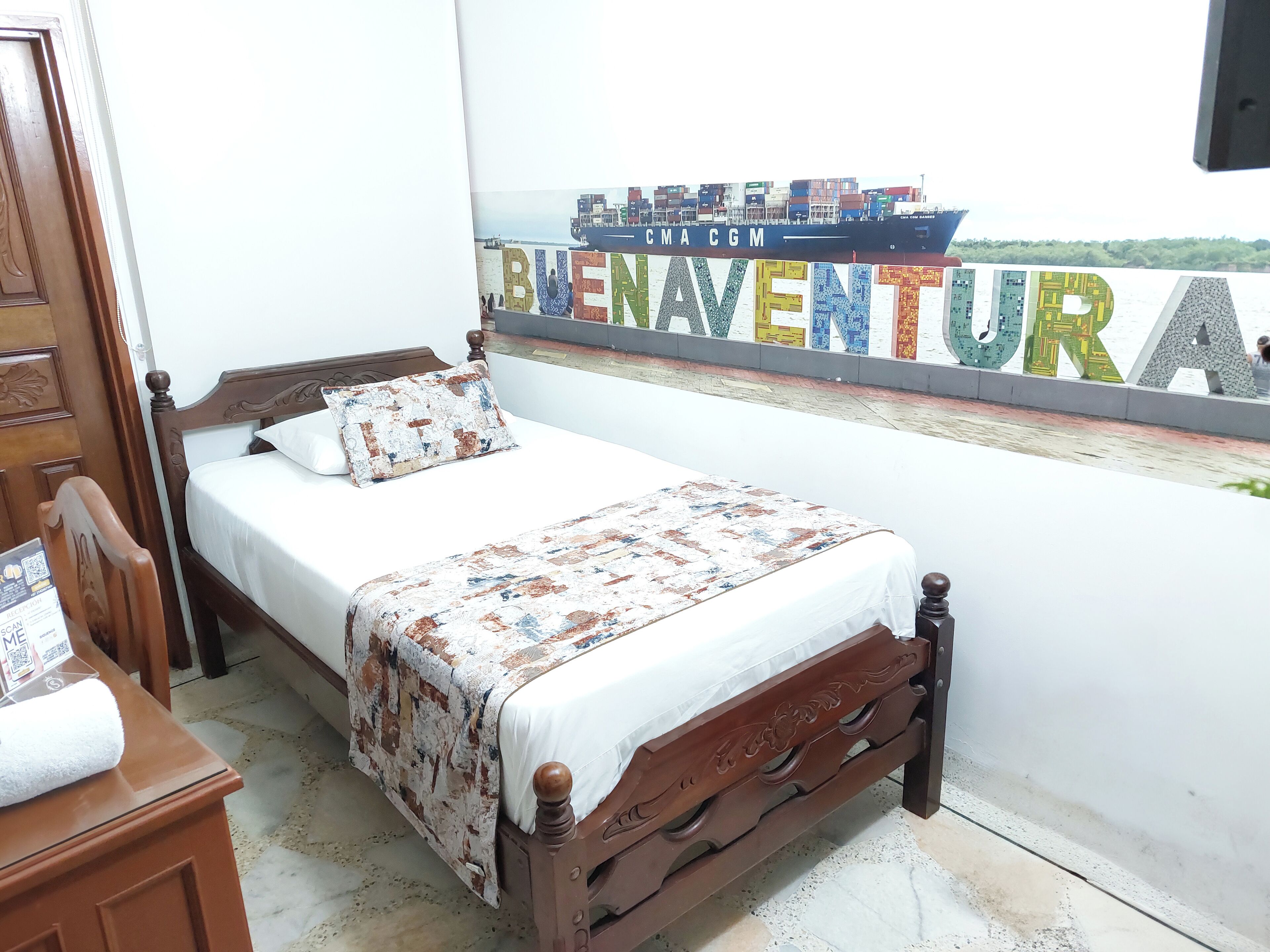 Quarto com uma cama, mesa de cabeceira de madeira e uma parede com uma janela grande.