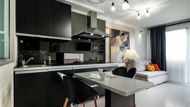 Uma cozinha moderna com armários escuros, uma ilha central e uma área de refeições com sofá e luminária.