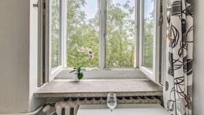 Uma janela com vista para árvores, uma planta em vaso e uma taça de vinho no parapeito.