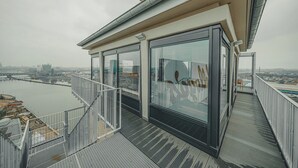 Um edifício moderno com grandes janelas de vidro e guarda-corpo metálico com vista para um rio.
