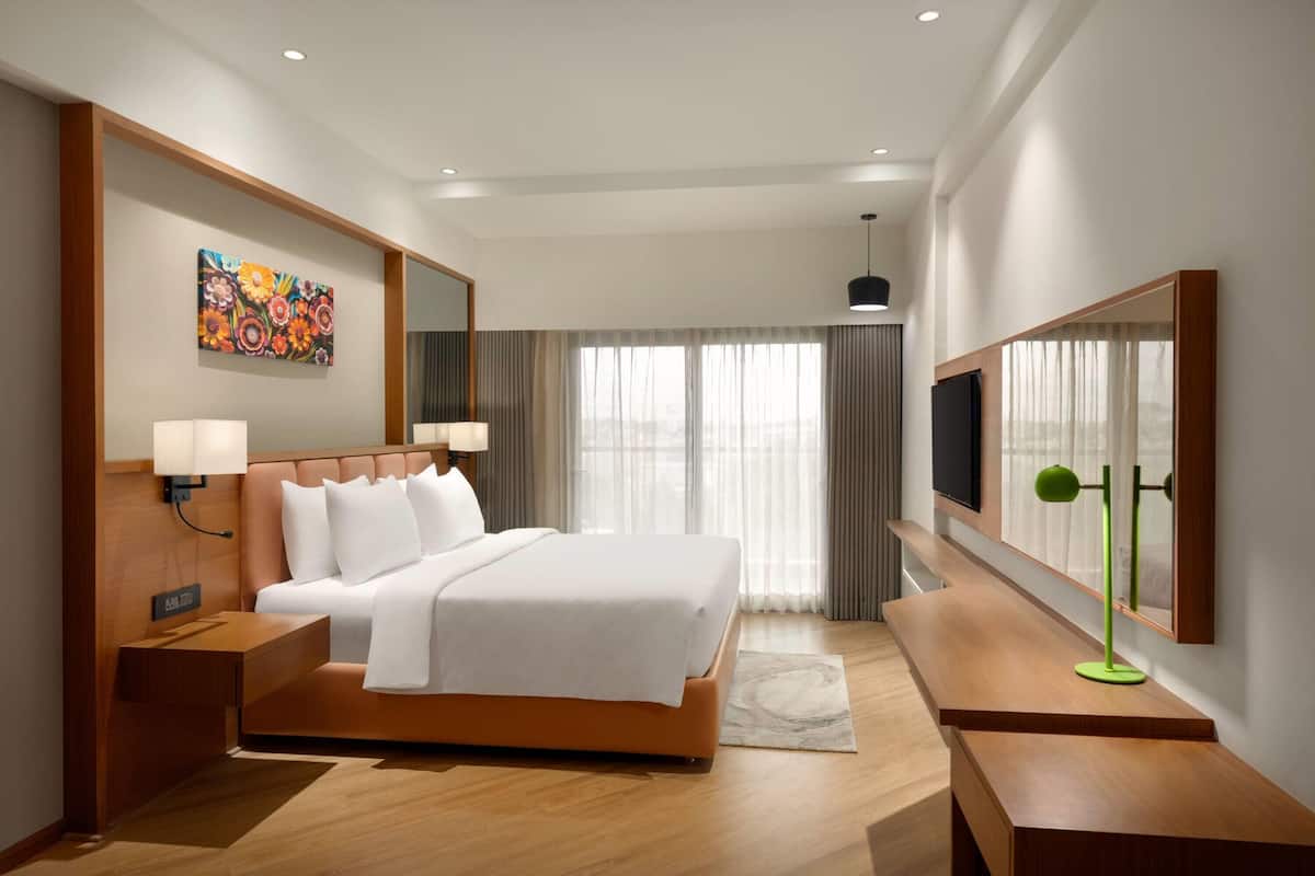 Quarto de hotel com uma cama grande, uma mesa de cabeceira, uma televisão e uma janela com cortinas.