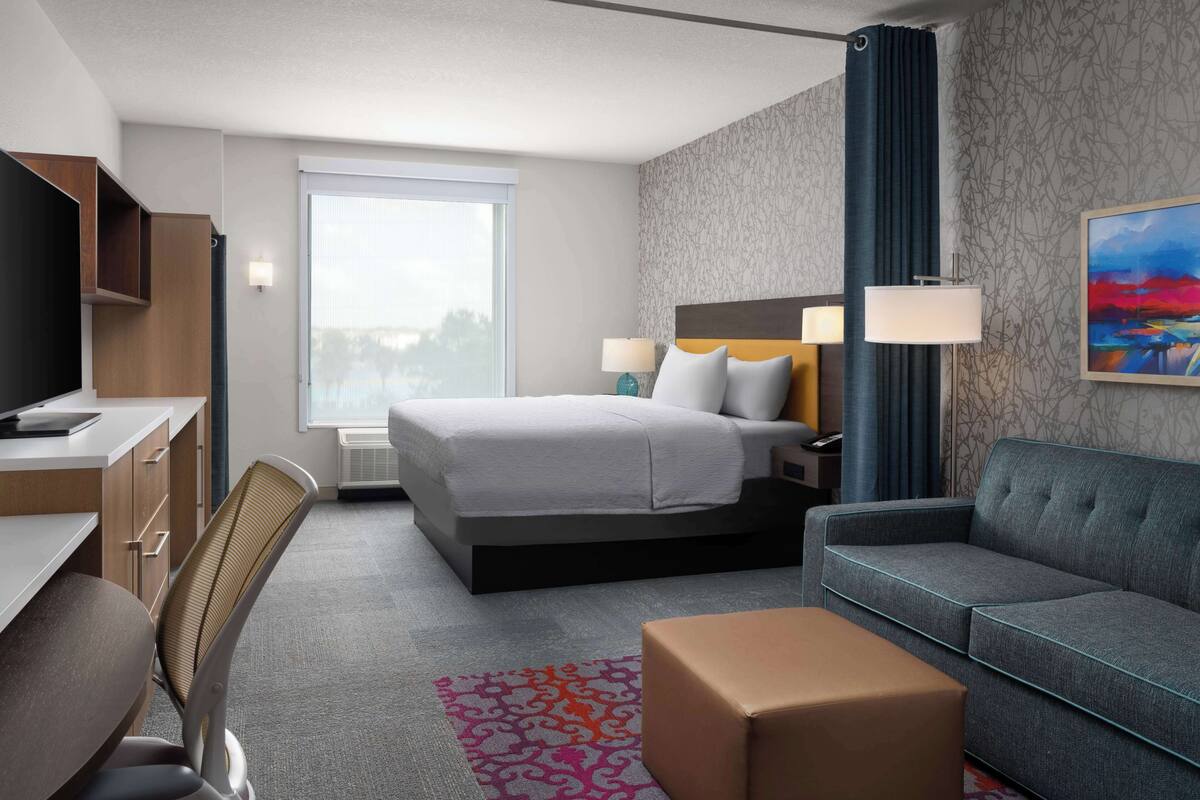 Quarto de hotel moderno com cama, sofá, escrivaninha e cadeira.