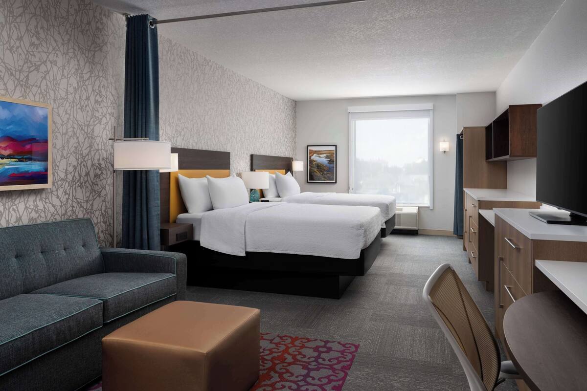Quarto de hotel com cama, sofá, escrivaninha e televisão.