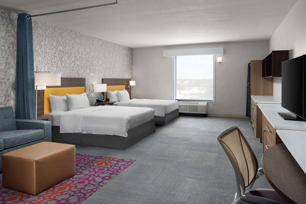 Quarto de hotel com duas camas, uma escrivaninha, televisão, uma cadeira e janela com vista.