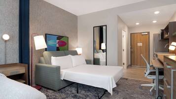 Quarto de hotel com cama, escrivaninha, cadeira, sofá, espelho e um quadro na parede.