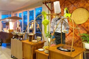 Cozinha com um chef preparando alimentos, um buffet com diversos pratos e uma parede rústica com cesta trançada.