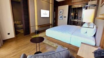 Quarto de hotel moderno com uma cama grande, uma mesinha de cabeceira com luminária, uma pequena mesa redonda e uma cadeira.