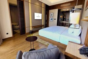 Quarto de hotel moderno com uma cama grande, uma mesinha de cabeceira com luminária, uma pequena mesa redonda e uma cadeira.