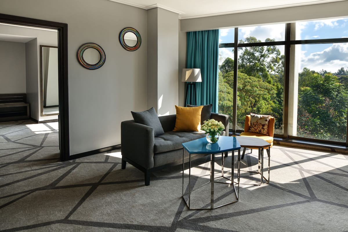 Sala de estar moderna com sofá, mesa de centro e vista para uma floresta através de grandes janelas.