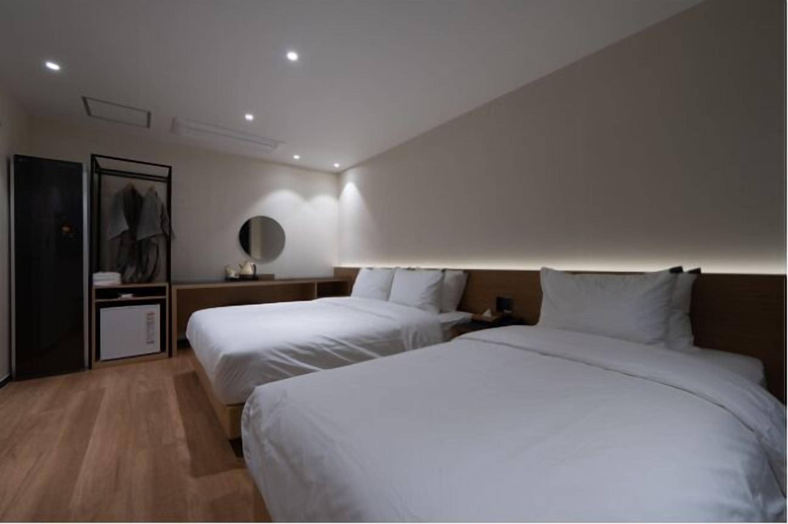 Quarto de hotel com duas camas, um guarda-roupa, um espelho e uma pequena mesa.