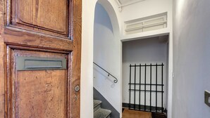 Uma porta de madeira com uma abertura para correspondência em metal, uma escadaria com corrimão metálico e um portão de metal preto.