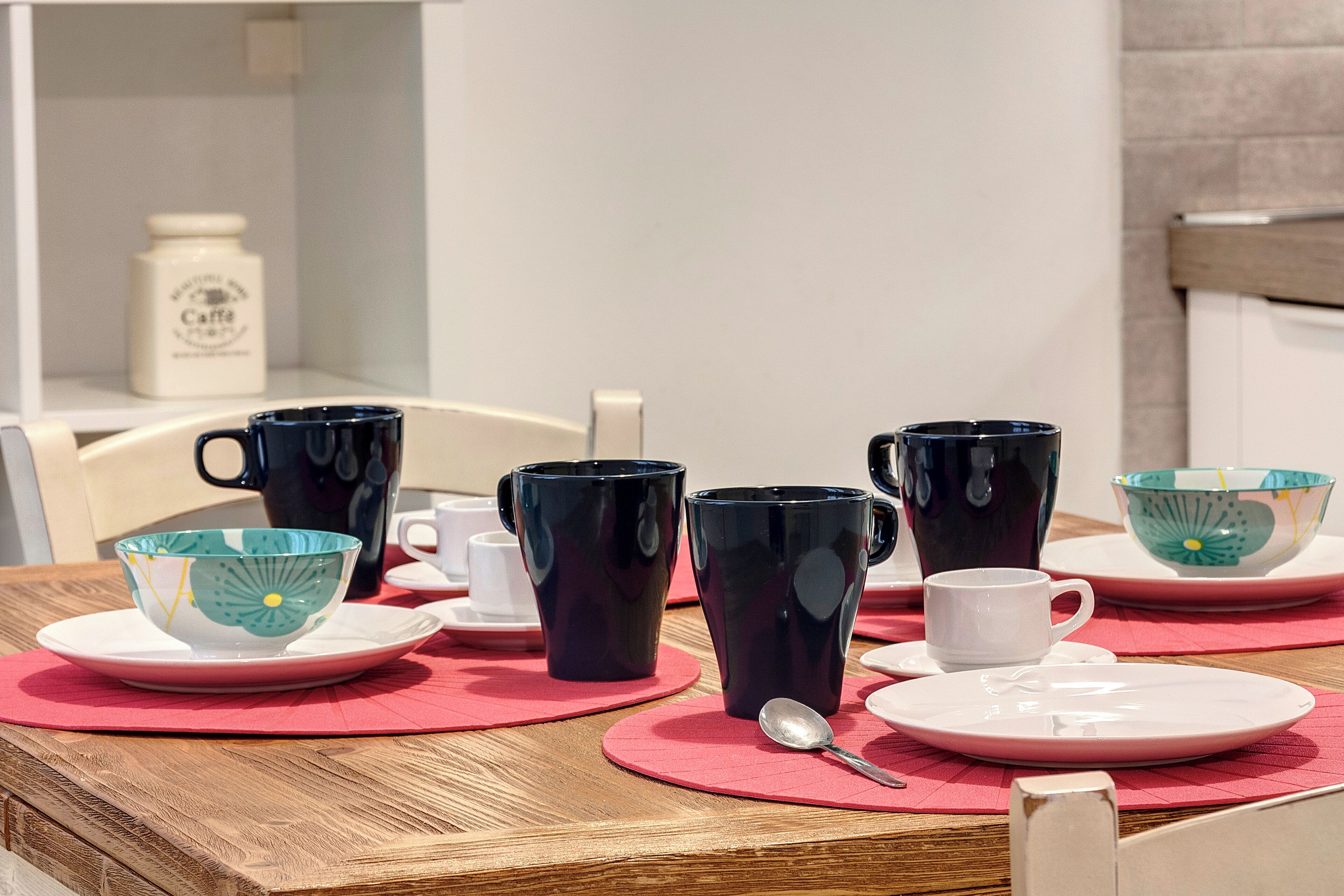 Uma mesa de jantar posta com vários copos e pratos, uma colher e uma garrafa com a inscrição "Caffe".