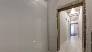 Um corredor com um espelho grande que reflete um quarto com soalho de madeira e uma porta.