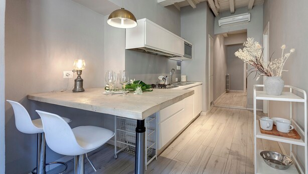 Uma cozinha moderna com armários brancos, um espaço bar com banquetas e uma luminária pendente.