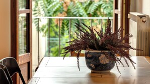 Uma planta em vaso sobre uma mesa de madeira, com vista para o verde através de uma janela.