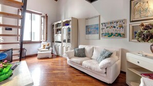 Uma sala de estar ampla com um sofá branco, piso de madeira, um armário branco e uma estante.