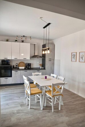Uma cozinha moderna com armários brancos, uma mesa de jantar com cadeiras brancas e um lustre.