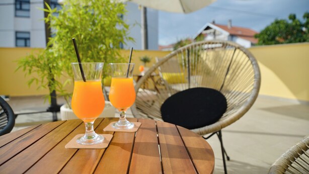 Dois copos de suco de laranja sobre uma mesa de madeira, com uma cadeira de vime ao fundo.