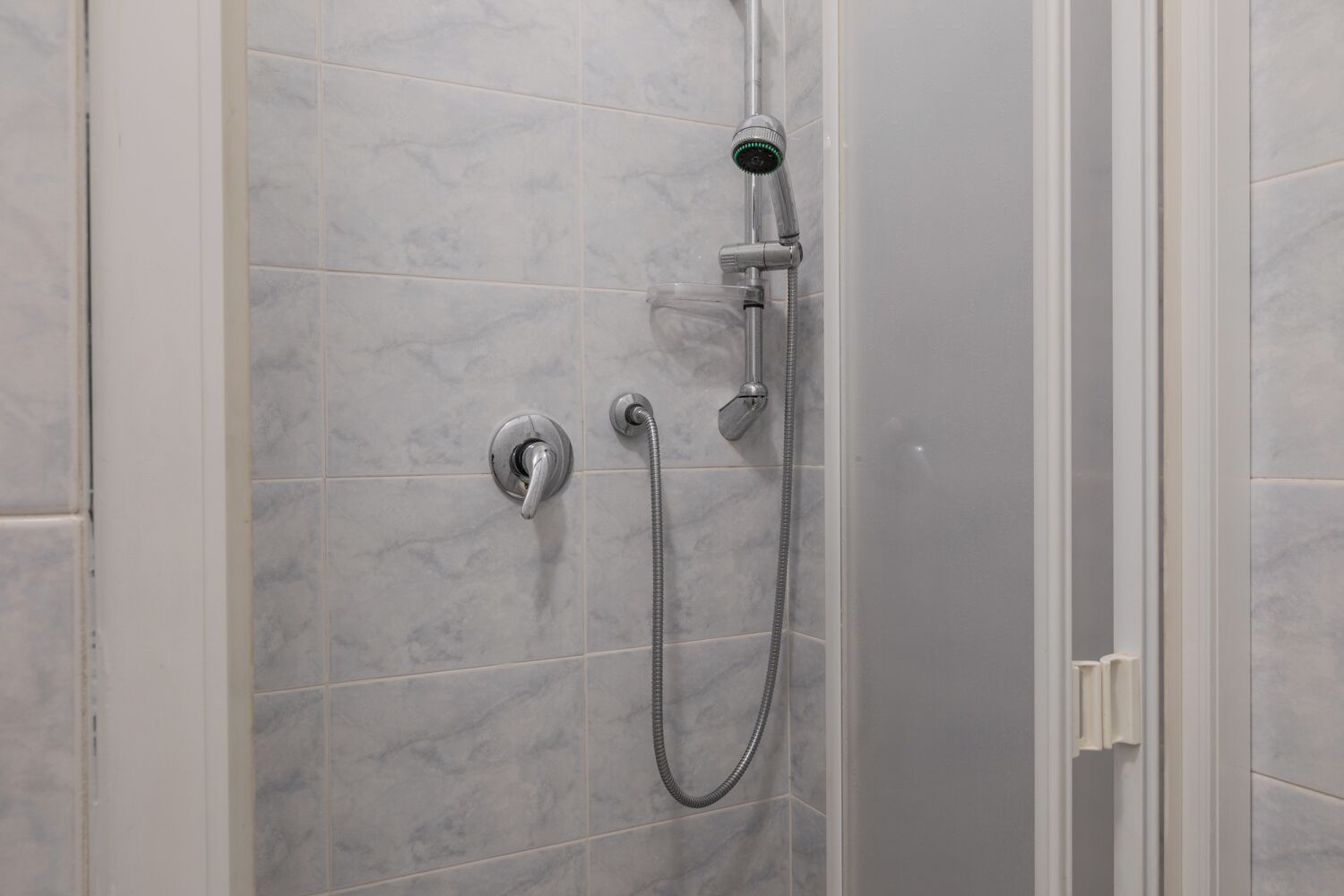 Chuveiro com chuveiro manual e chuveiro fixo, ambos instalados em uma parede revestida de azulejos.