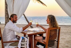 Um casal sentado à mesa de madeira numa praia, com vista para o oceano.