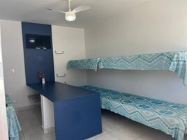 Quarto compacto com beliches, uma pequena escrivaninha e ventilador de teto.