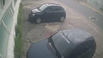 Um carro preto estacionado na rua, com um edifício de um lado.