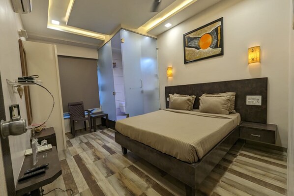 Quarto de hotel moderno com uma cama grande, uma escrivaninha com cadeira, um guarda-roupa e um quadro na parede.