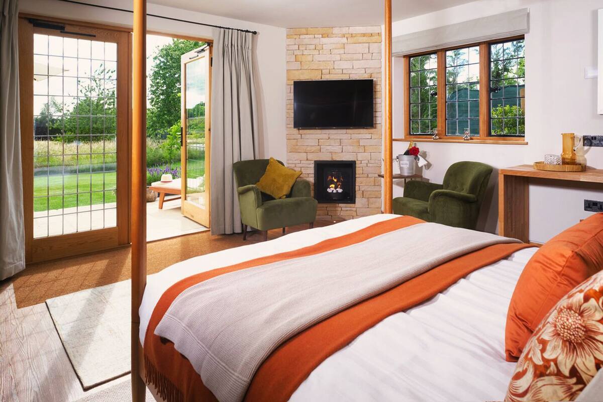 Quarto com uma cama grande, lareira, televisão e vista para um jardim através de uma porta deslizante.