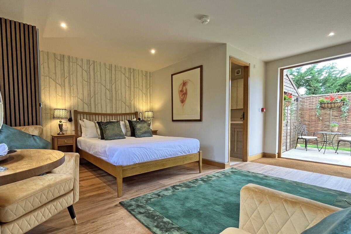 Quarto com cama, mesas de cabeceira, uma cadeira, tapete e vista para o exterior.