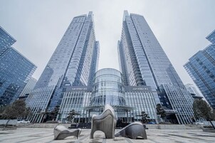 Um edifício moderno com fachada de vidro, apresentando uma estrutura circular central e duas torres altas.