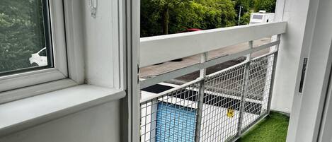 Uma varanda com guarda-corrimão branco, vista para uma árvore e um vaso azul no chão.