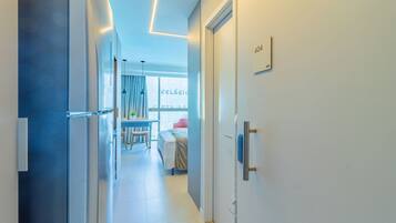 Corredor moderno de hotel com área de refeições, uma cama e porta com número de quarto.