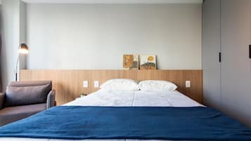 Quarto de hotel com cama, cadeira, abajur e obras de arte na parede.