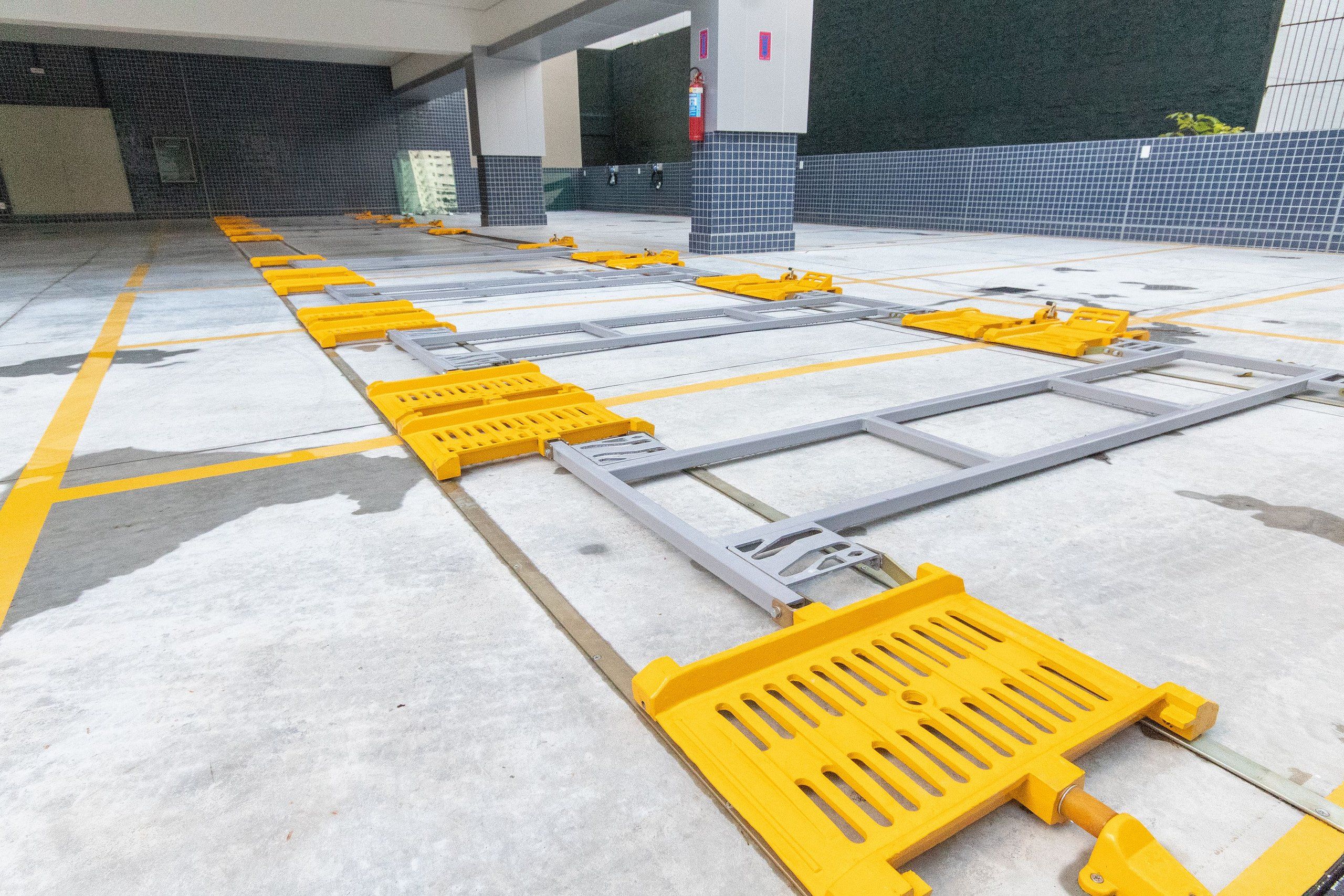 Uma garagem de estacionamento com barreiras amarelas e estruturas de metal cinzento no chão.