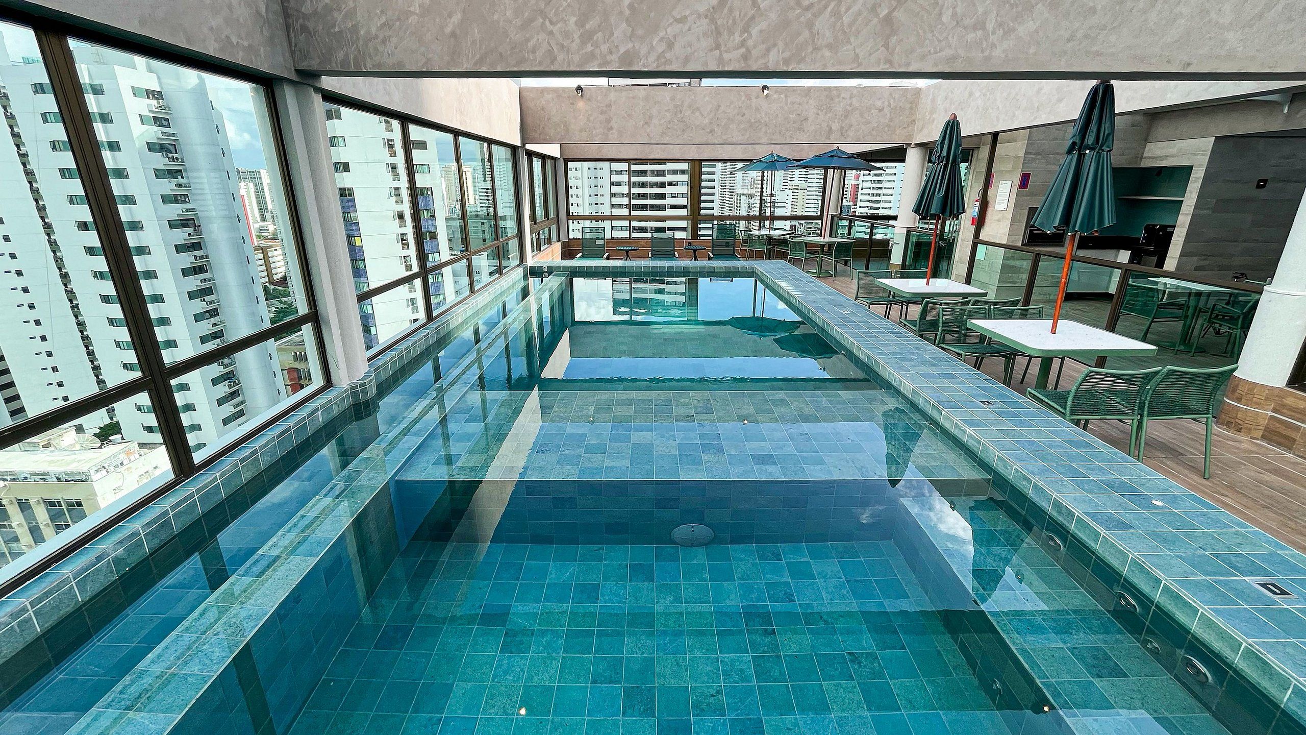 Uma piscina interior moderna com paredes de vidro transparente, vários níveis e áreas de estar ao ar livre.