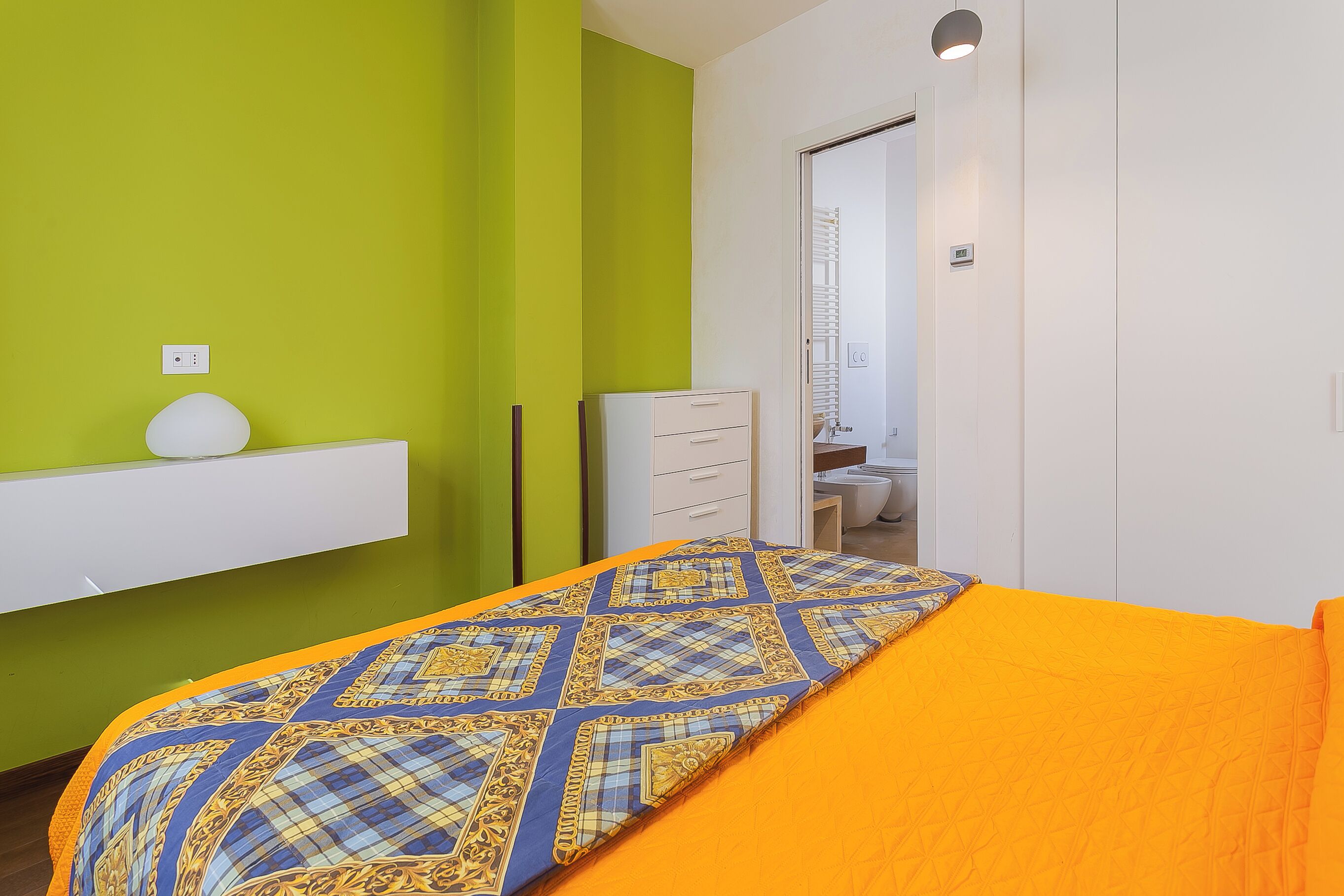 Quarto com cama, penteadeira branca, parede verde e porta branca.