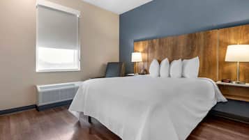 Quarto de hotel com uma cama grande, cabeceira de madeira, duas luminárias de cabeceira, janela com persianas e aquecedor fixado na parede.