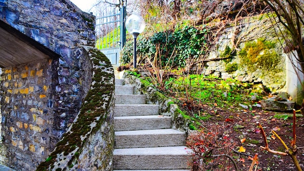 Uma escadaria de pedra leva a um edifício com um portão de metal e um poste de luz.