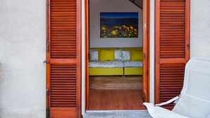 Um quarto com porta de madeira, um sofá amarelo e uma pintura de flores.