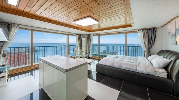 Quarto moderno com uma cama grande, pequena área de cozinha e varanda vista para o mar.