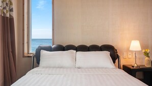 Quarto de hotel com cama, mesa de cabeceira com abajur e vista para o mar.
