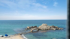 Uma paisagem costeira com um afloramento rochoso, uma ponte e uma praia.