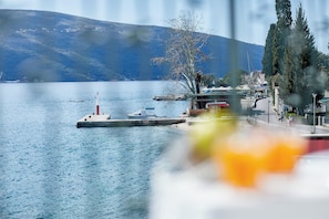 Um lago com barcos atracados num cais, um farol e uma árvore em primeiro plano.