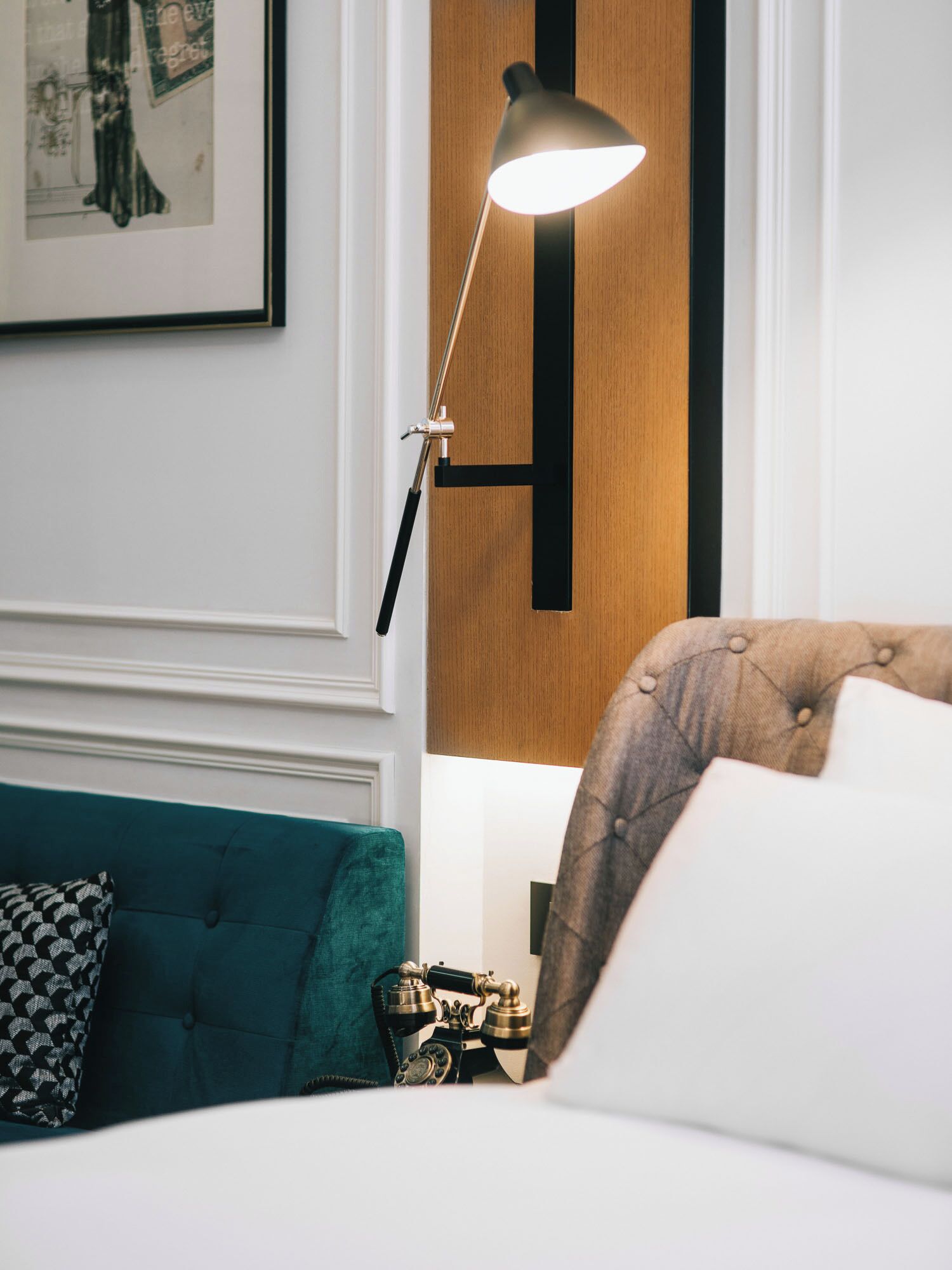 Quarto de hotel bem organizado com um sofá azul-turquesa, um abajur clássico e um telefone antigo.