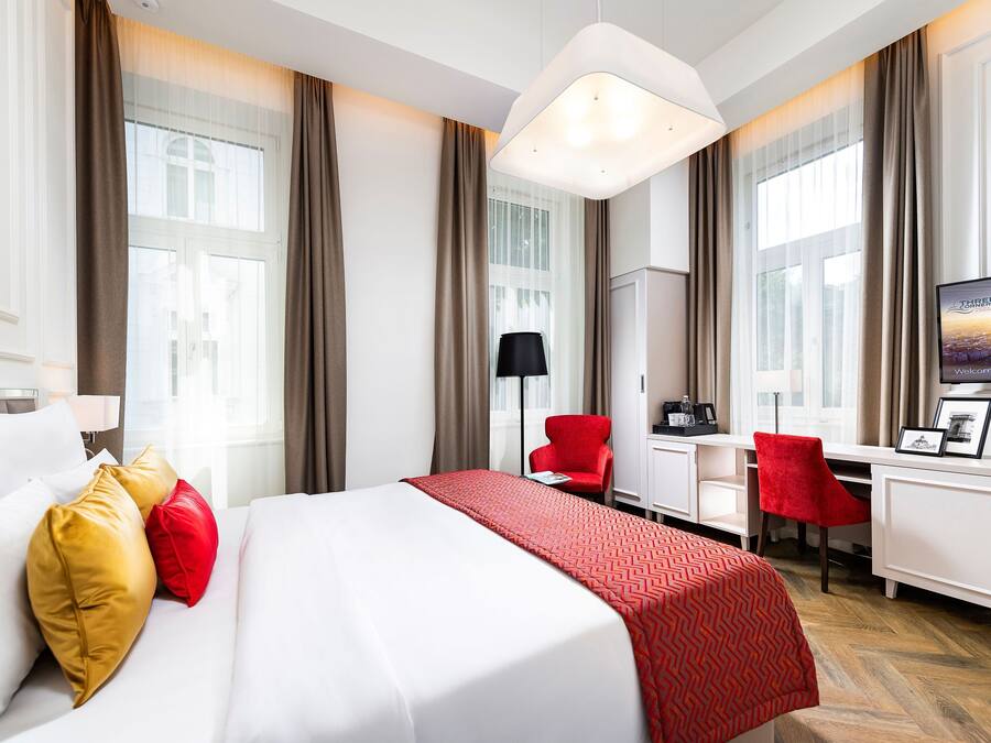 Quarto de hotel com cama, escrivaninha, cadeira e televisão.