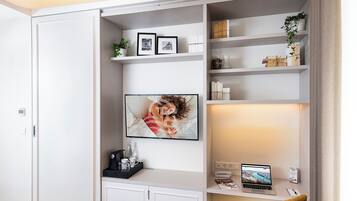 Quarto de hotel com uma cama, uma escrivaninha com um laptop, uma cadeira e uma TV fixada na parede.