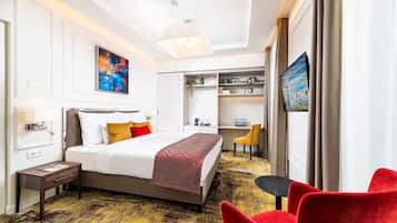 Quarto de hotel com cama, escrivaninha, cadeira e televisão.